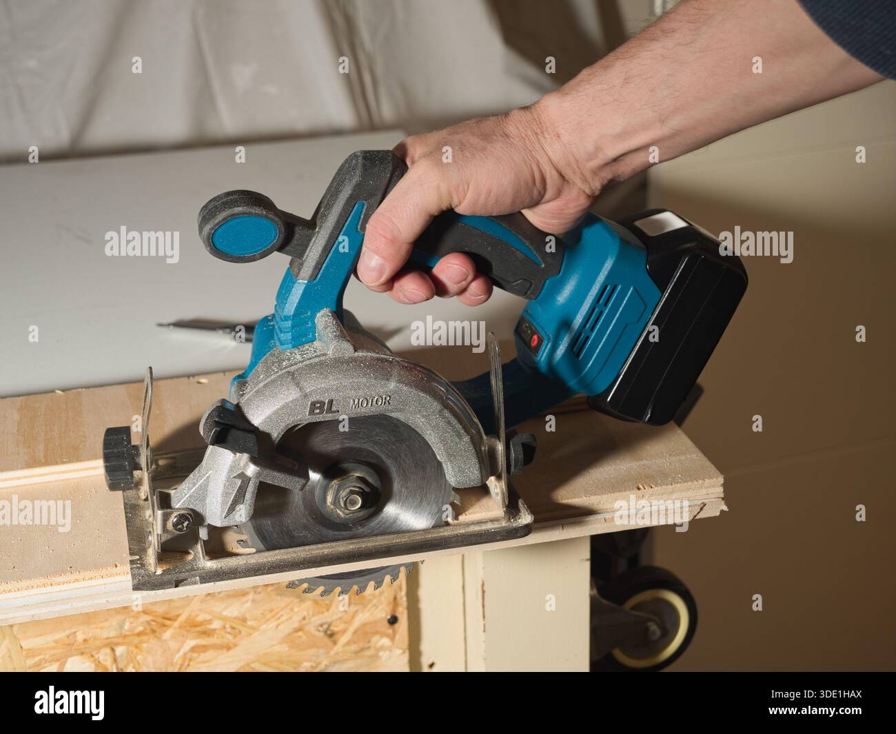 Hand Using Cordless Circular Saw to Cut Plywood; Close-up of a worker's ...