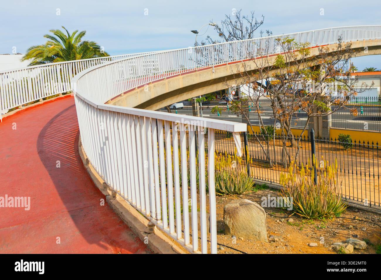 Curving elevated pedestrian walkway with red surface and metal railings ...