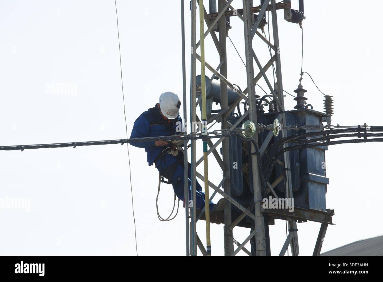 Utility lineman inspecting transformer on tower, wearing blue coveralls ...