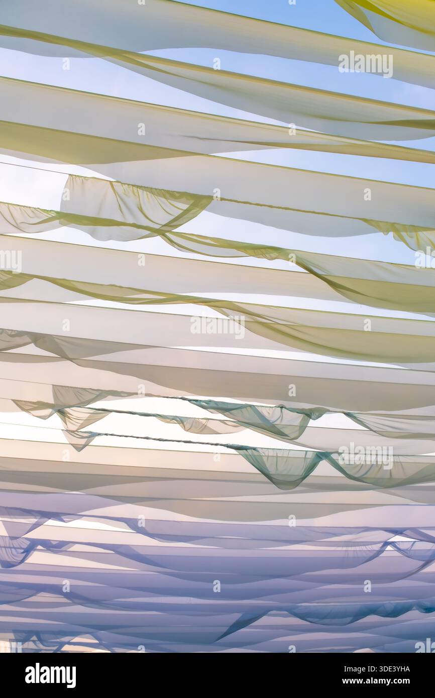 translucent, white and pale yellow fabric strips suspended in the air ...