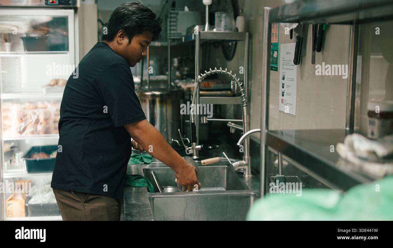 Chef washing dishes in a commercial dark kitchen, working at stainless ...