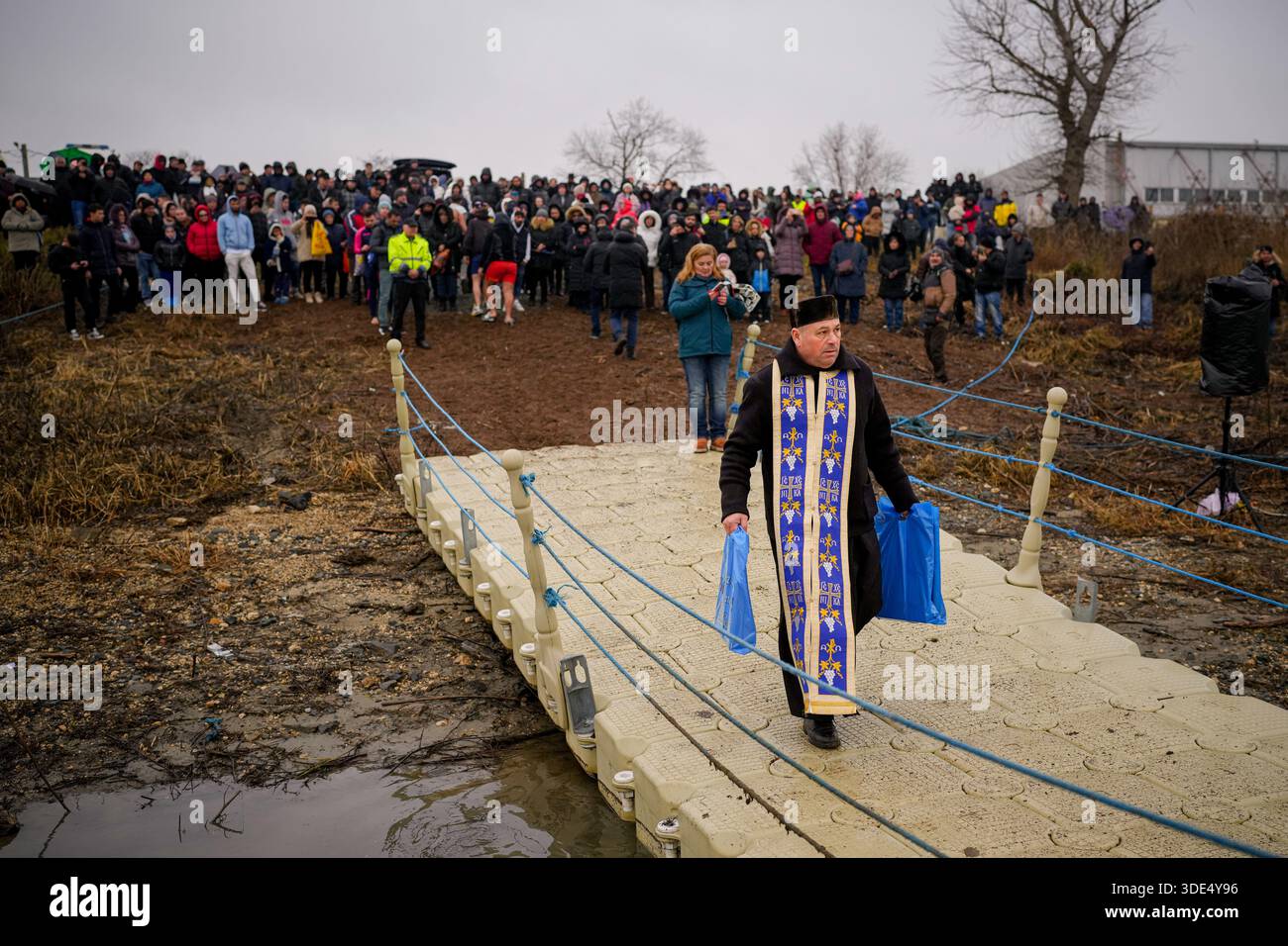 An Orthodox cleric walks on a pontoon as people line up on a bank of ...