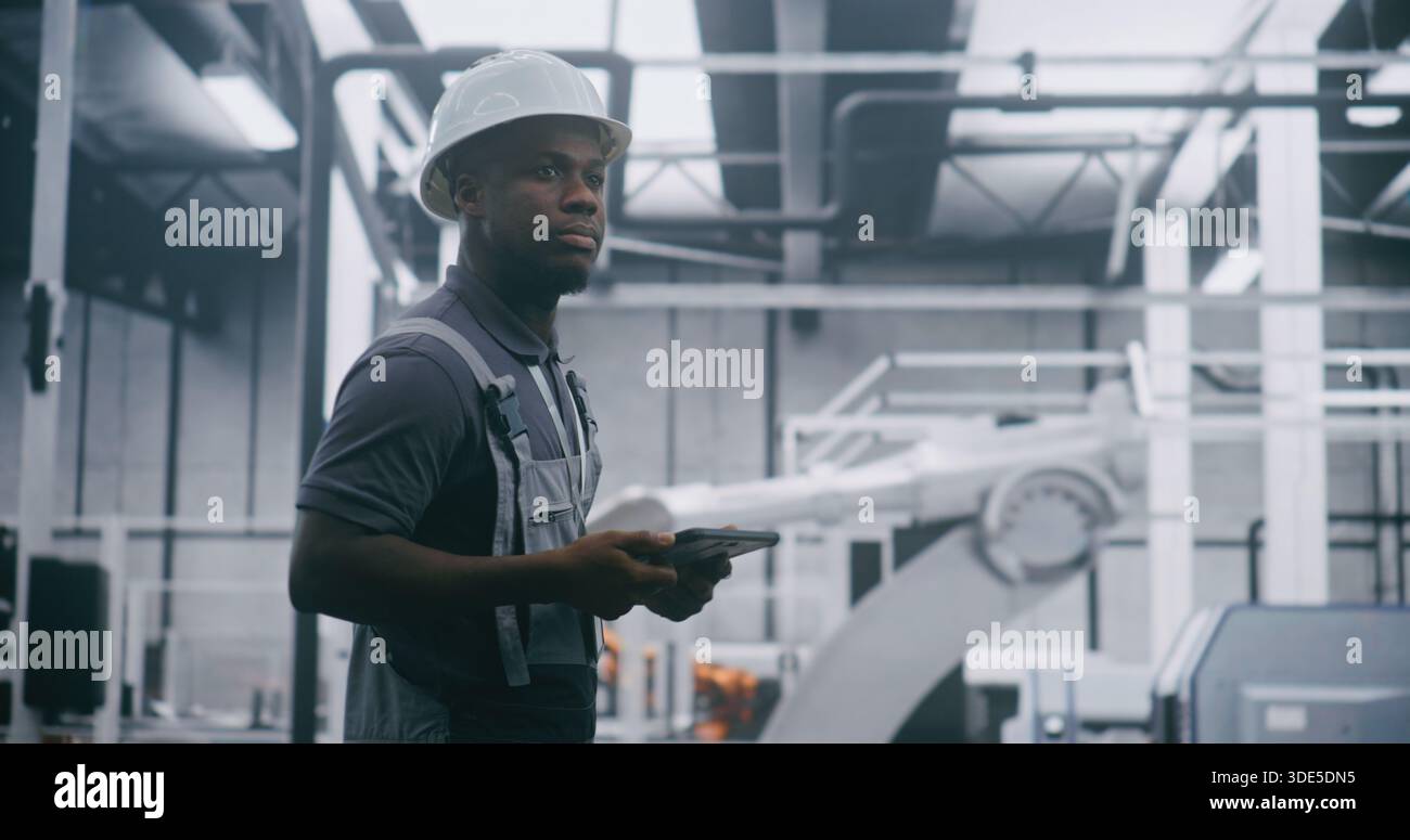 African American Factory Worker in Hard Hat Uses Handheld Device While ...