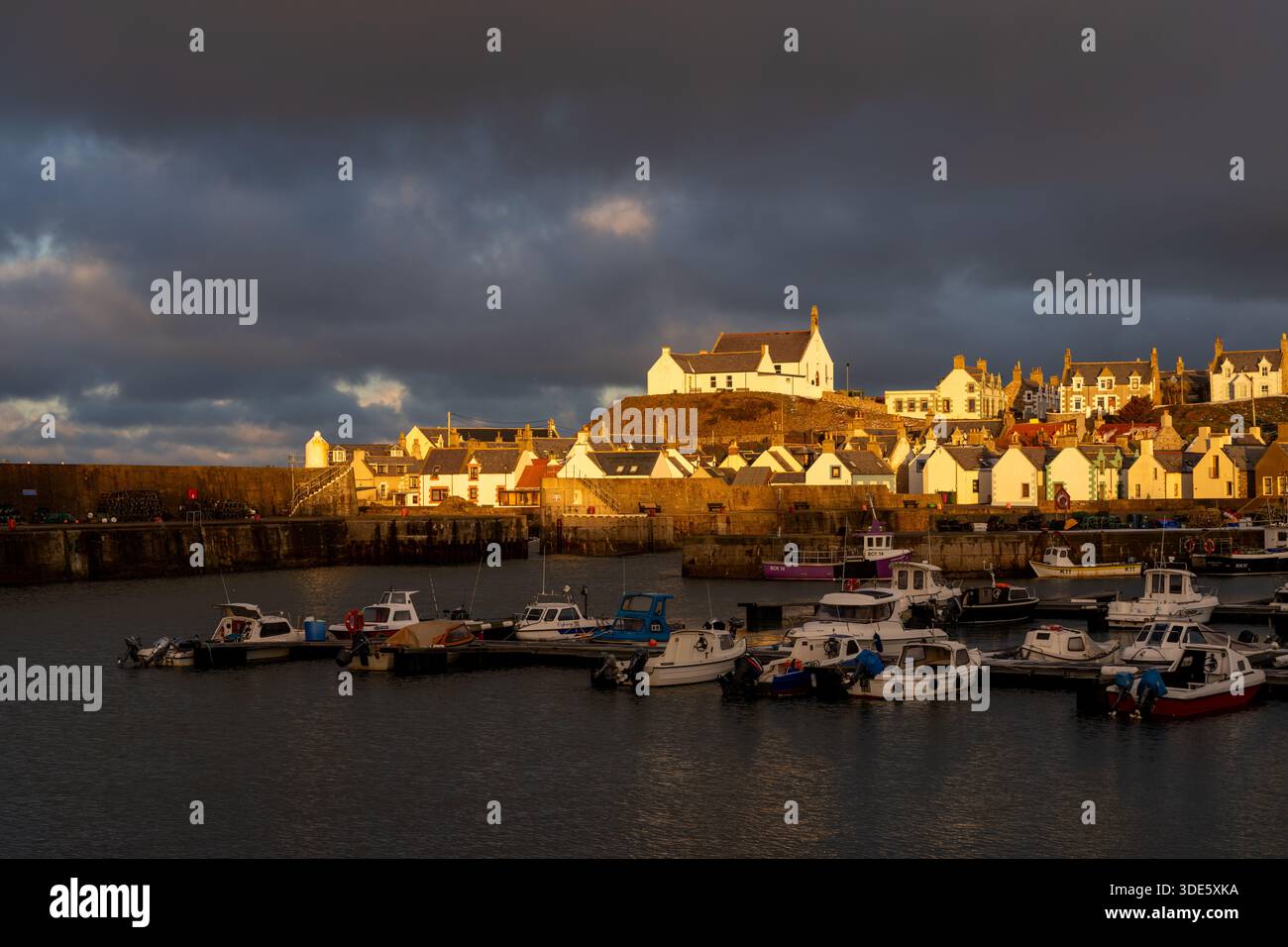 The sun sets over Findochty Harbour, casting warm light on boats and ...