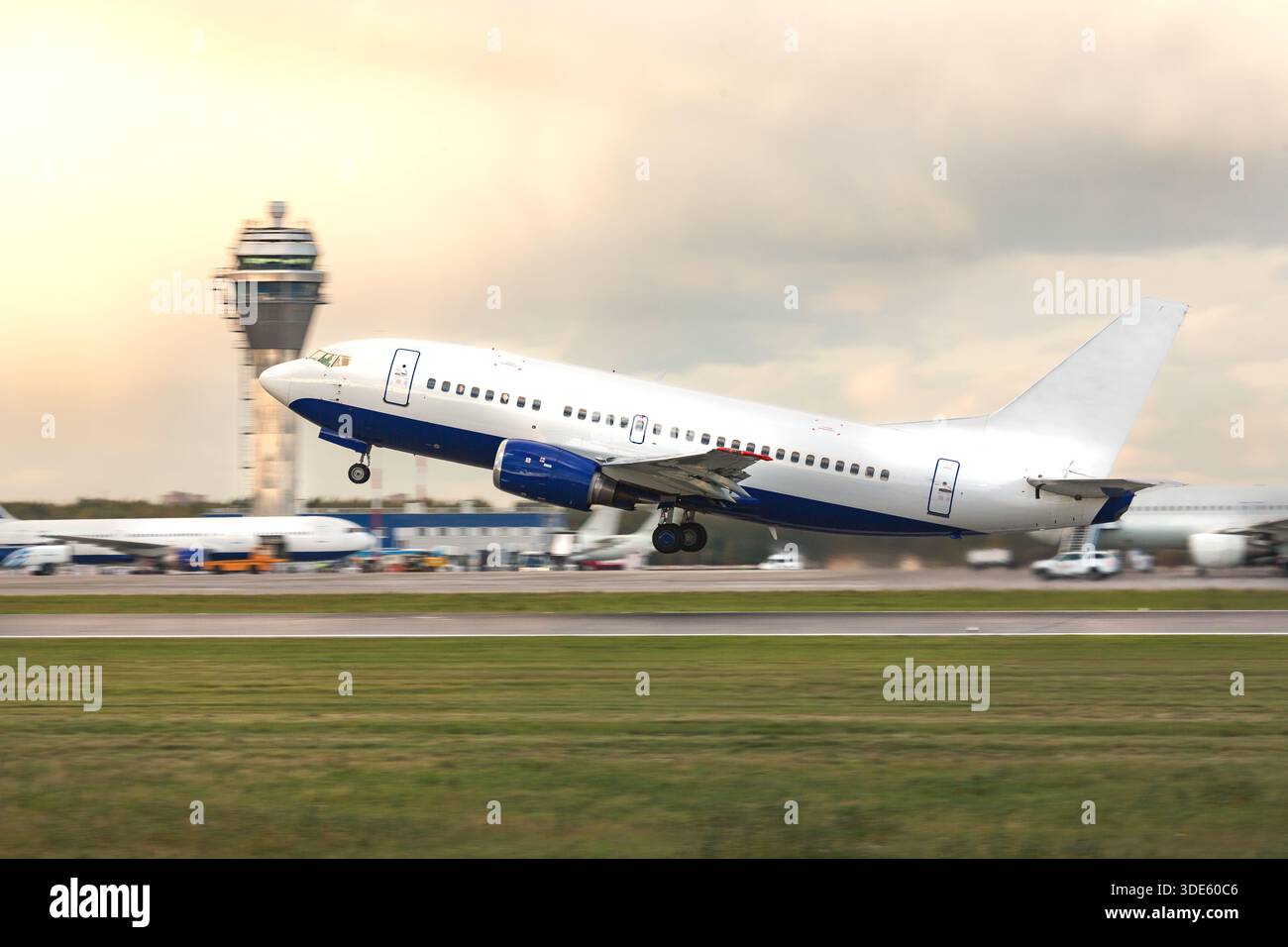 Narrow-body passenger modern airliner taking off from runway at sunset ...