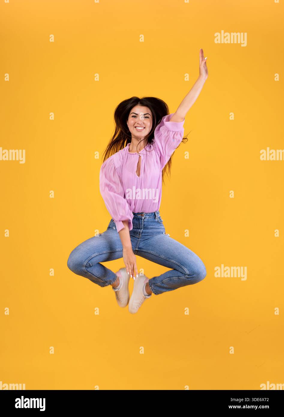 Joyful armenian woman jumping and touching legs with hand, yellow ...