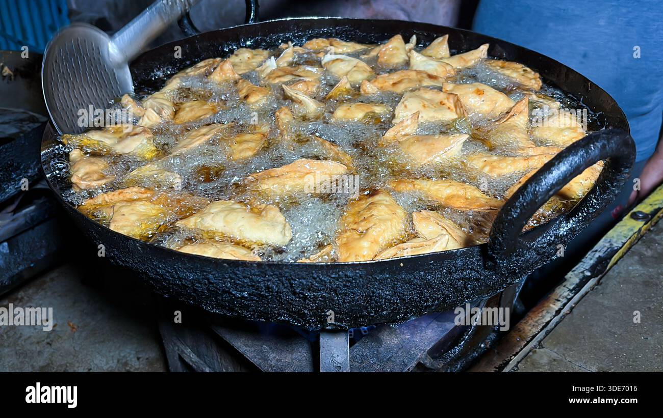traditional indian samosa deep frying in large iron pan at street shop ...