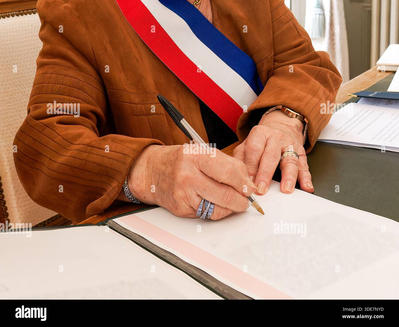 French mayor wearing a tricolor sash signs an official document at a ...