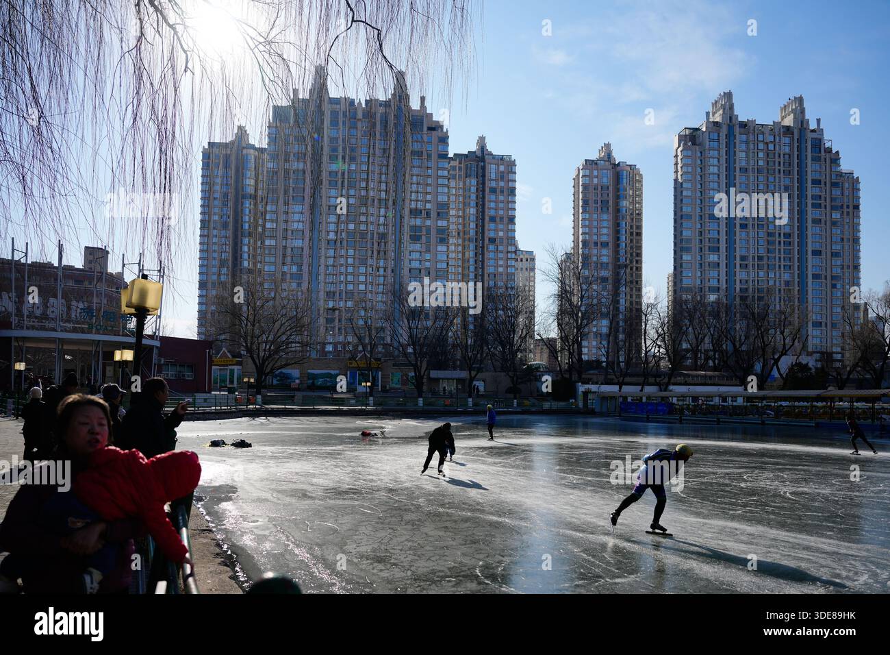 People skate on a frozen lake at Chaoyang Park in Beijing, with the ...