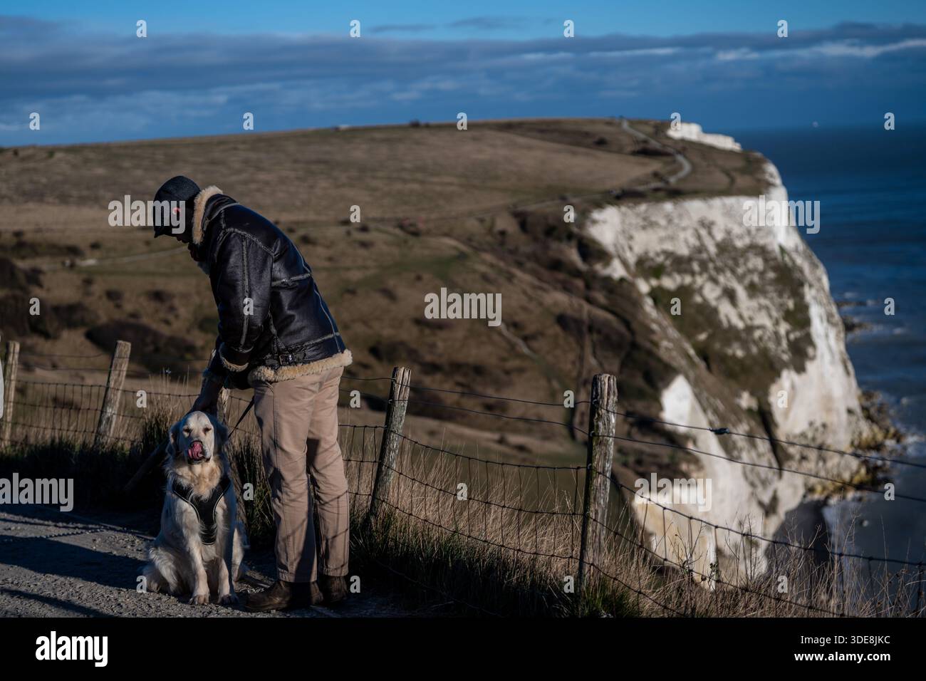 A man petting a dog at the white cliffs of Dover during sunset on ...