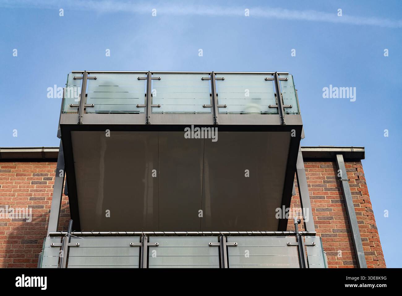 A modern balcony is seen above a brick building. The balcony has glass ...