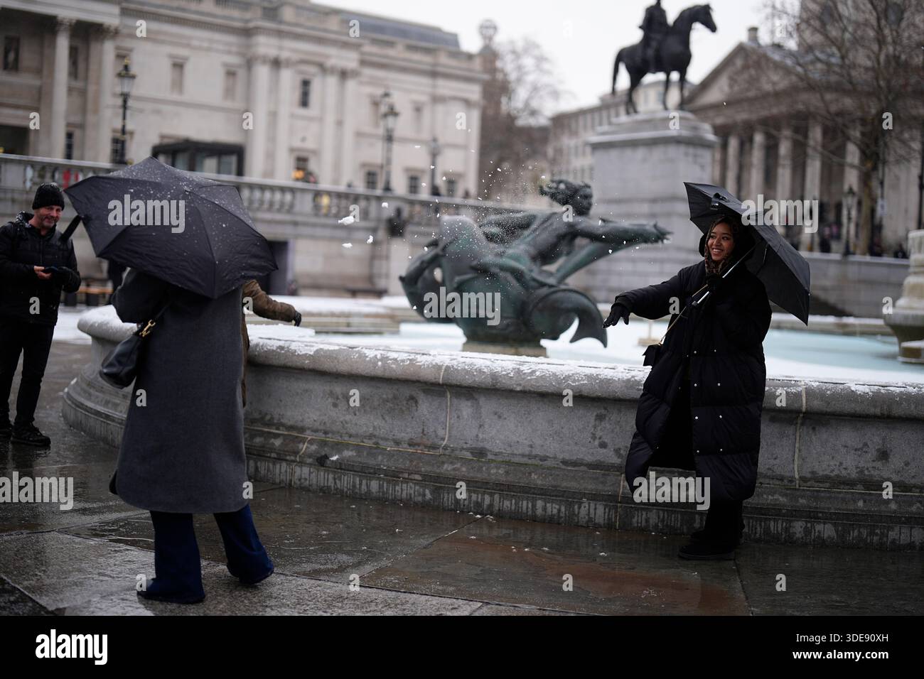 A woman throws a snowball in the falling snow in Trafalgar Square ...