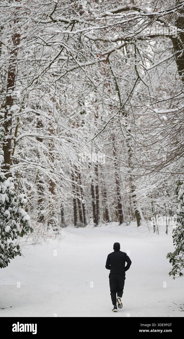 06 January 2026, Hamburg: A jogger runs along a path through the snow ...