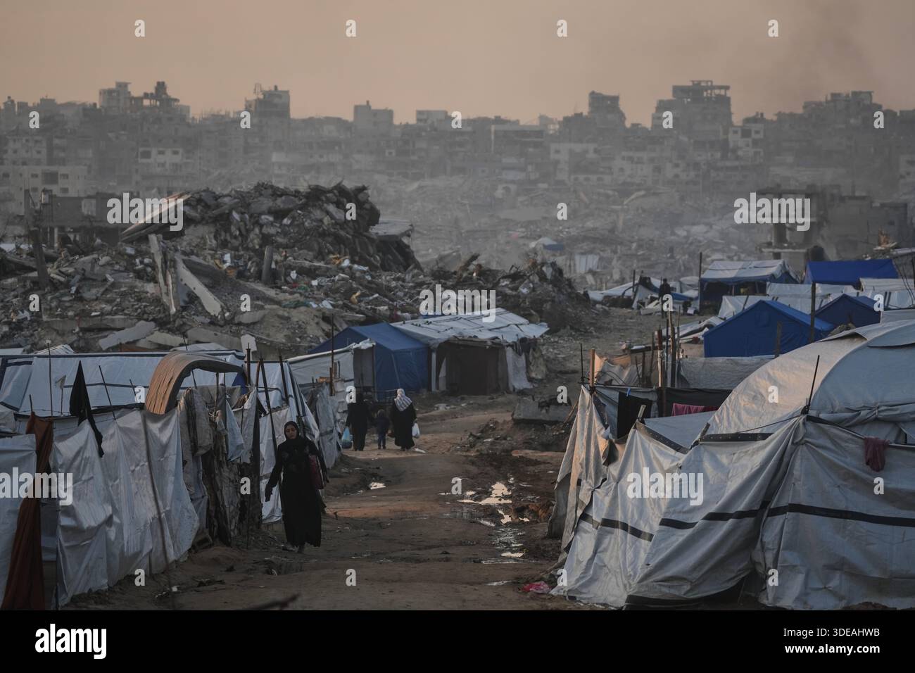 Palestinians walk past a tent camp amid buildings destroyed by Israeli ...