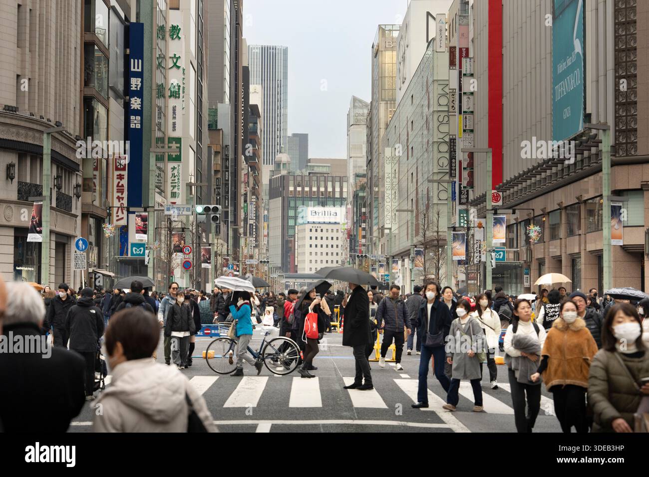 People cross the street in Ginza, Tokyo, under umbrellas. The iconic ...