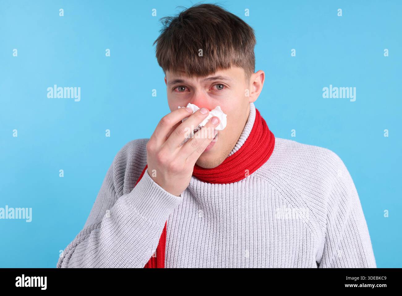Sick man with tissue suffering from cold on light blue background. Red ...