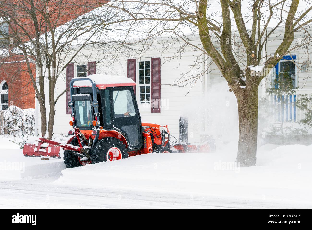 Small tractor fitted with a plow and snowblower clears snow from a ...