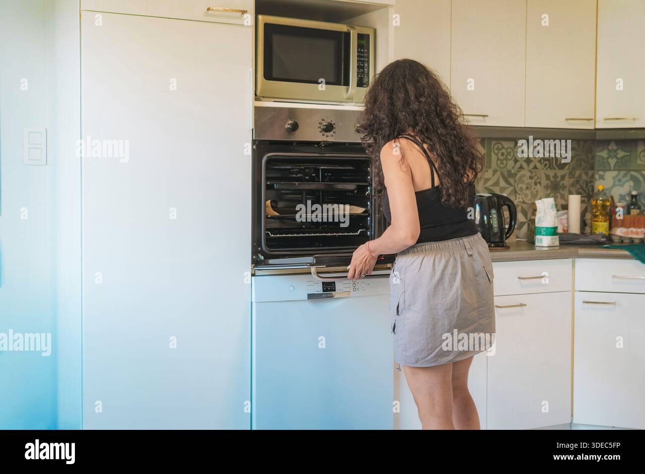 Middle-aged woman in her kitchen baking, she is opening the oven, in ...