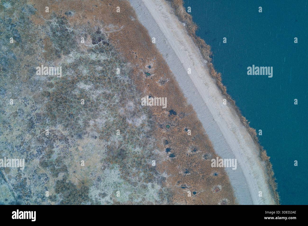 Top-down aerial view of a diagonal gravel embankment separating deep ...