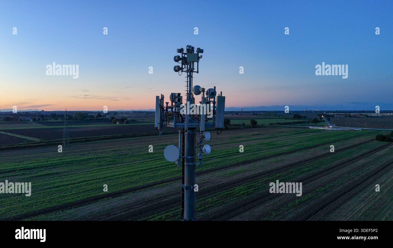 Cell tower stands tall in the countryside at dusk. Antennas and dishes ...