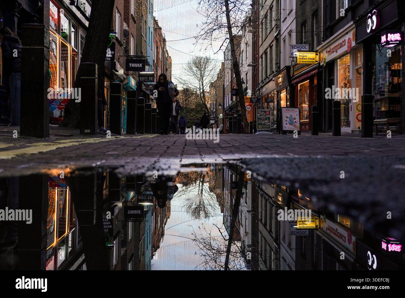 People are reflected into a puddle in a street in the area of Covent ...