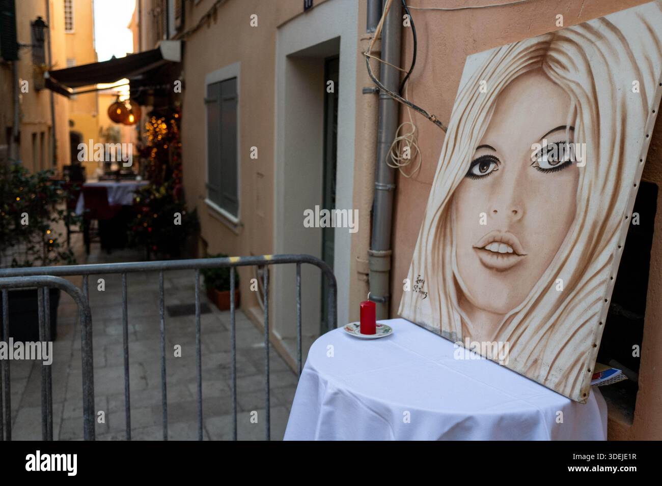 A painted portrait of Brigitte Bardot and a candle seen in an alleyway ...