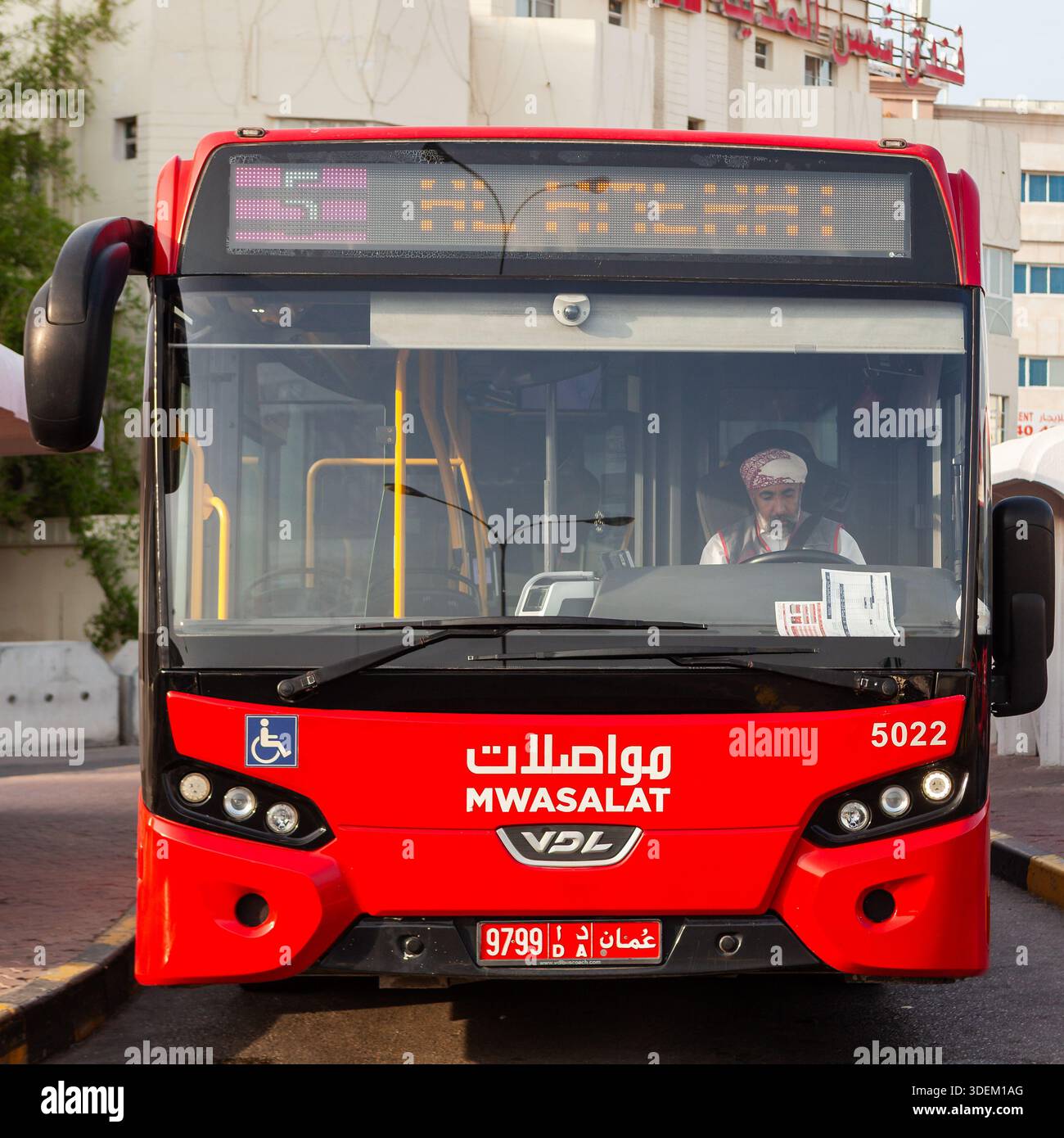 Red public bus in Muscat, Oman, with Mwasalat branding. The driver is ...