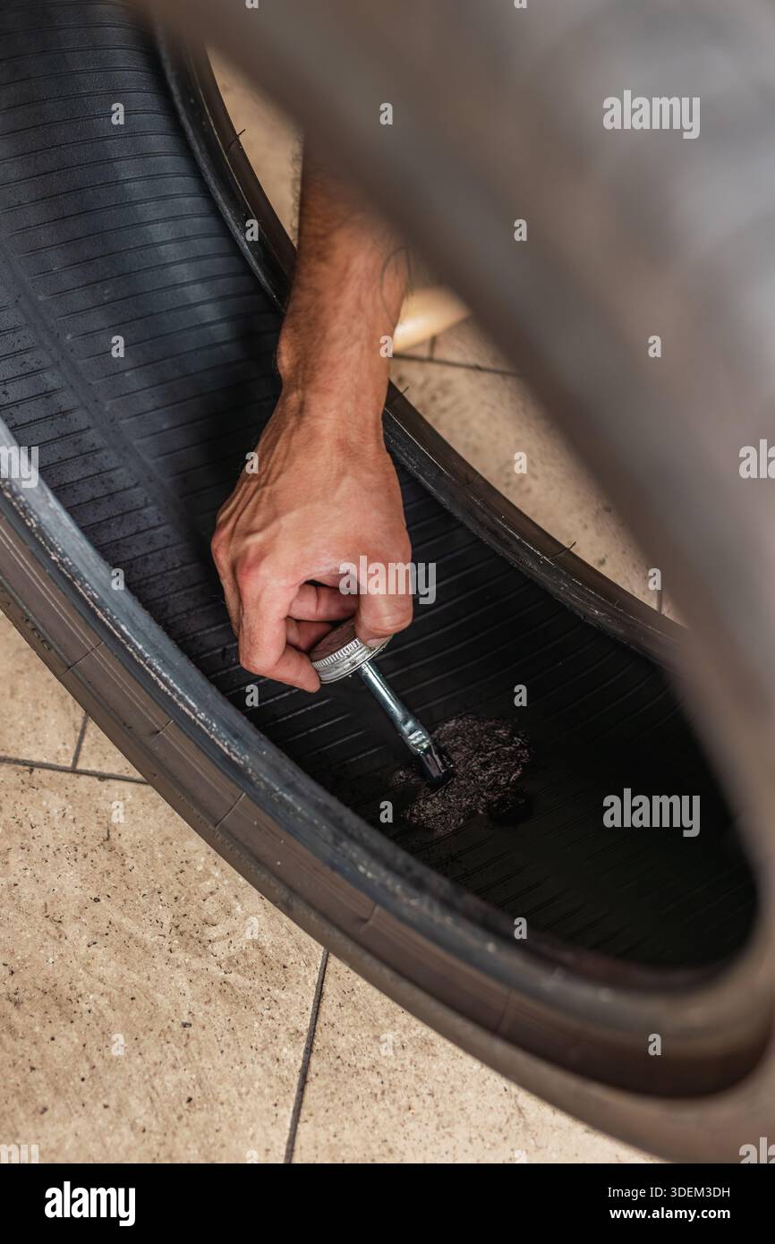 Tire specialist applying vulcanizing cement to repair a punctured tire ...