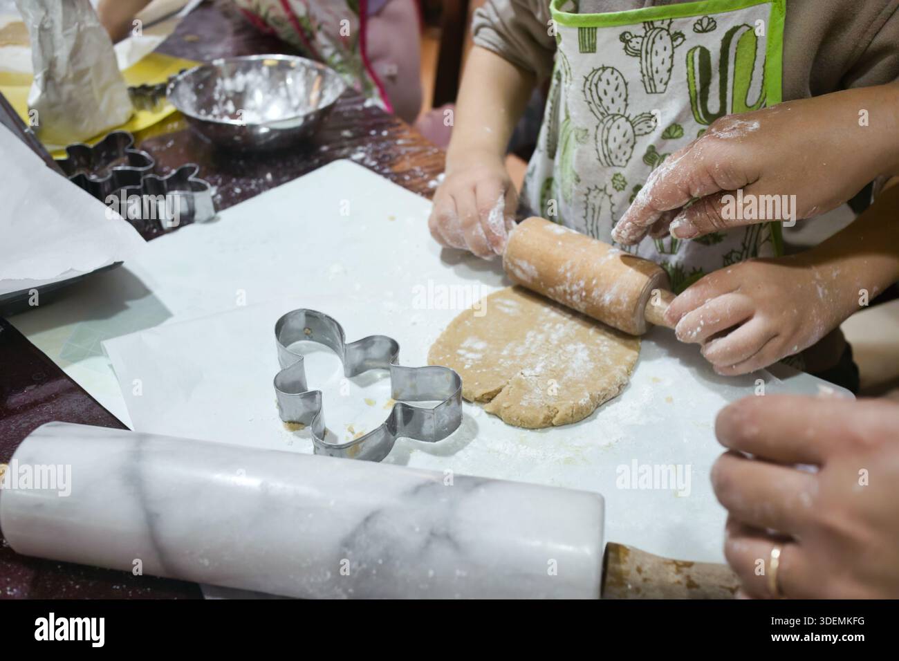 Close-up of a kid with his mother rolling pastry dough to make cut-out ...