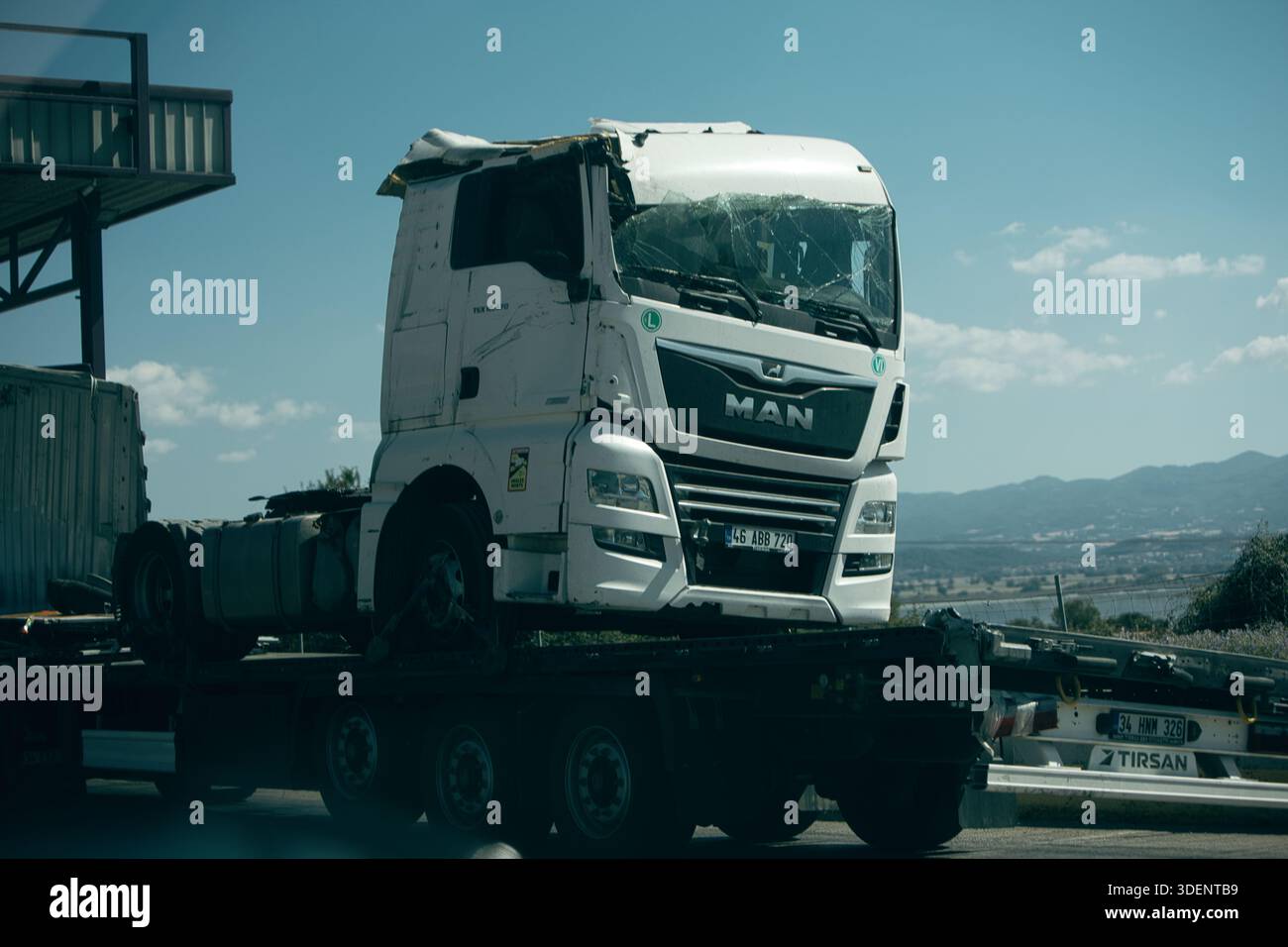 Damaged heavy-duty truck transported on a flatbed trailer along a ...