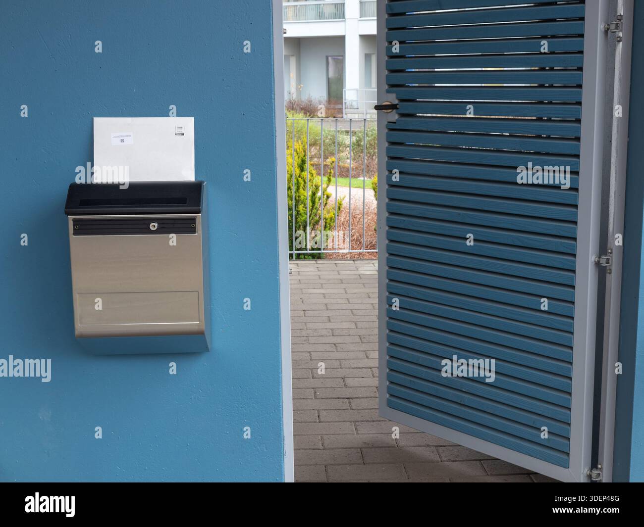 A modern, stainless steel wall-mounted mailbox with a black top flap ...
