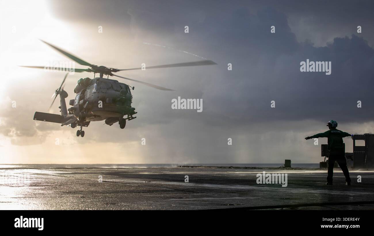 A U.S. Sailor signals to an MH-60R Sea Hawk helicopter, attached to ...