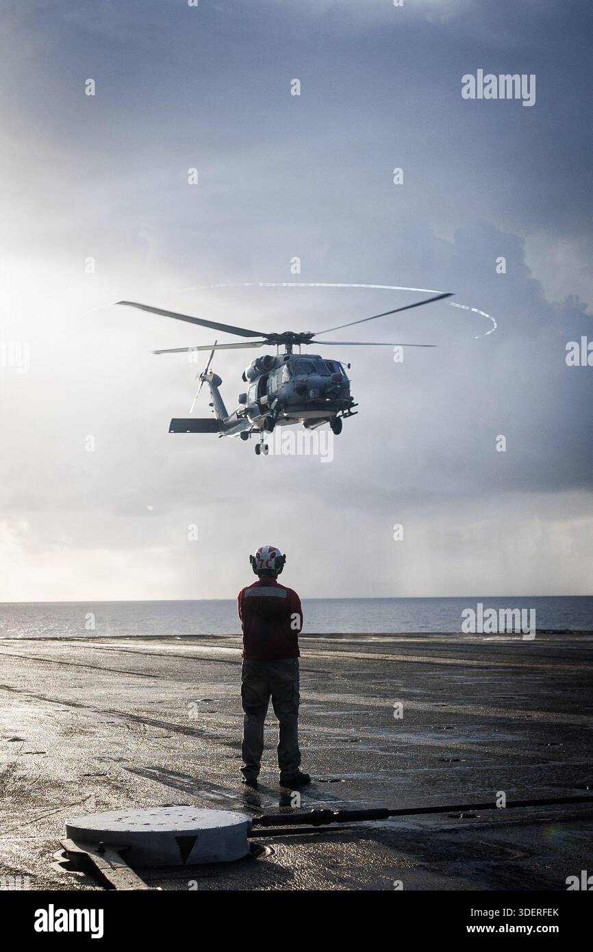 A U.S. Sailor observes the landing of an MH-60R Sea Hawk helicopter ...