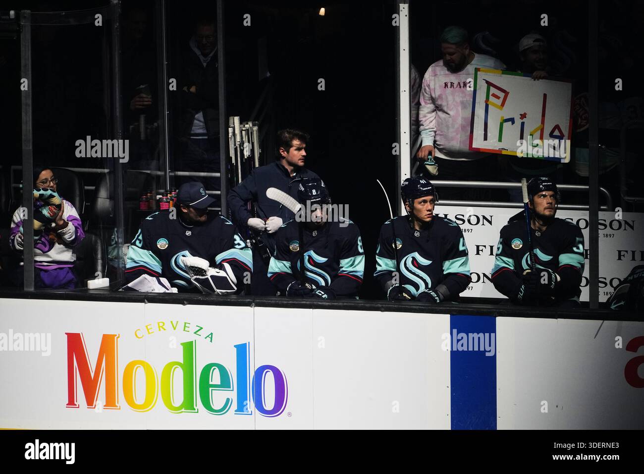A fan holds a sign for Pride night as the Seattle Kraken bench looks on ...