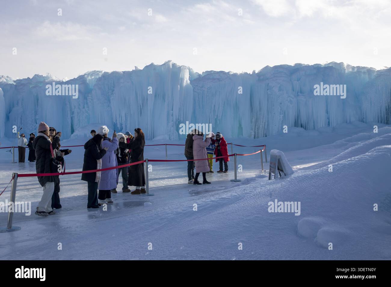 Tourists visit the blue ice waterfalls formed by frozen lake water at ...