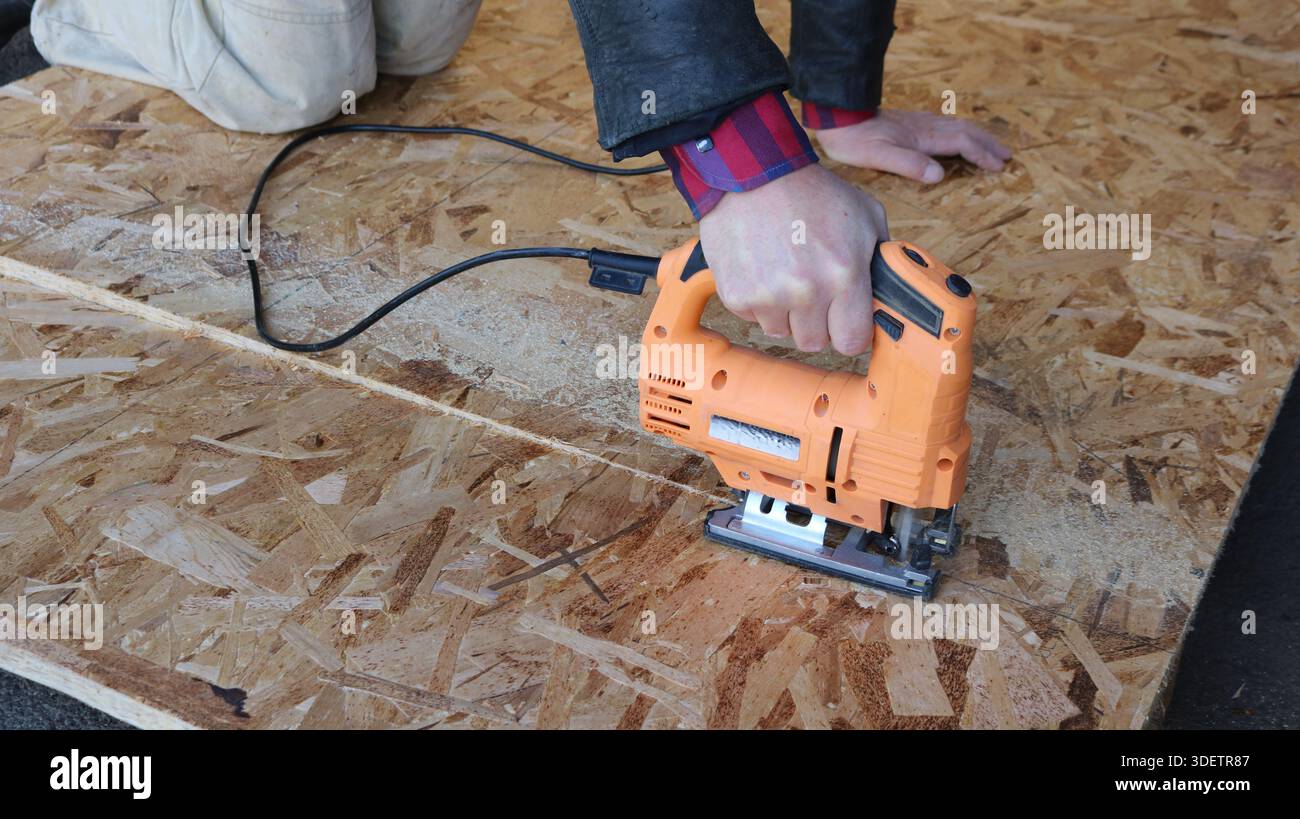 A partially visible white man kneeling with an orange electric jigsaw ...