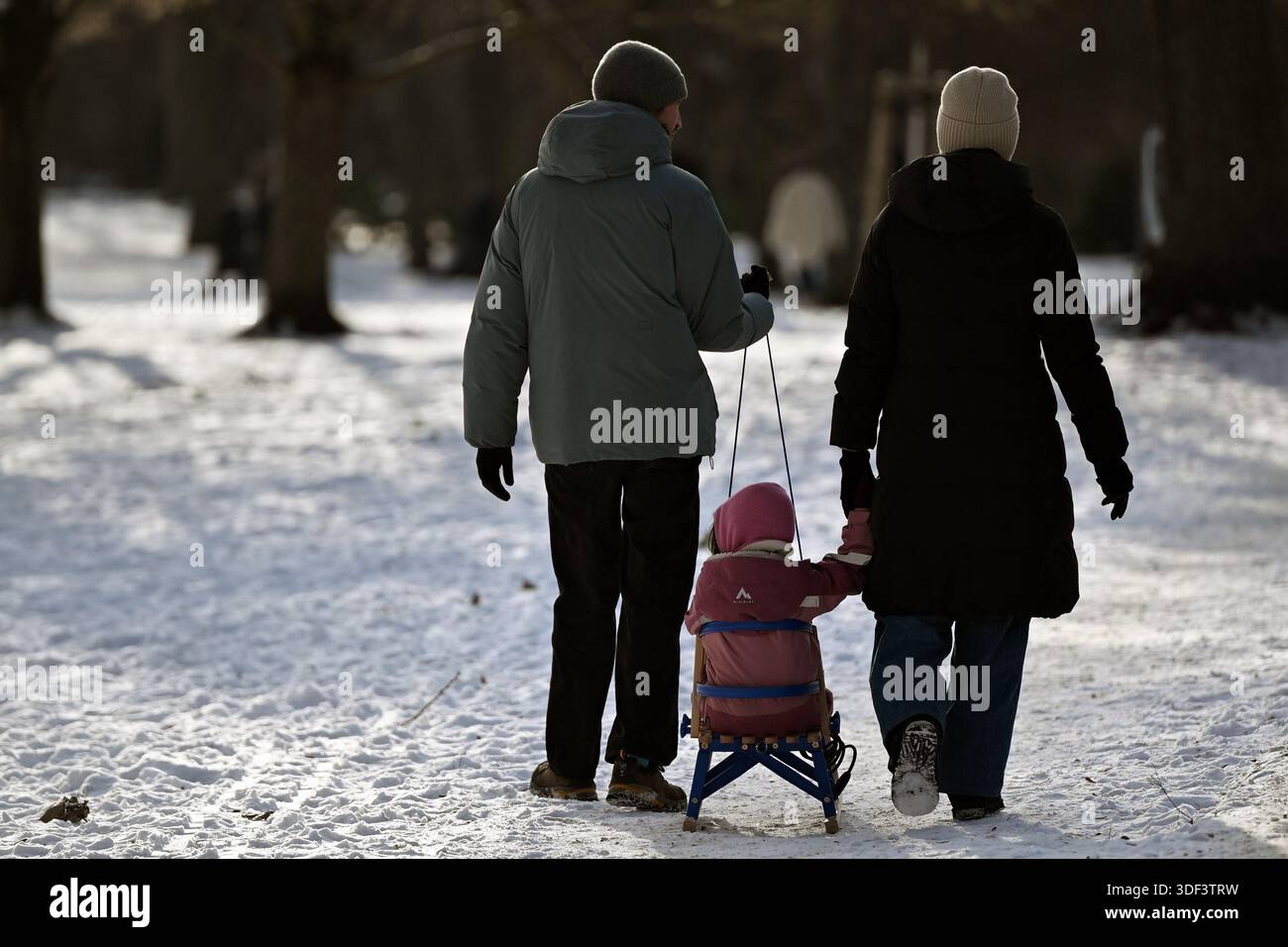 10 January 2026, Berlin: Two people pull a small child on a sledge ...