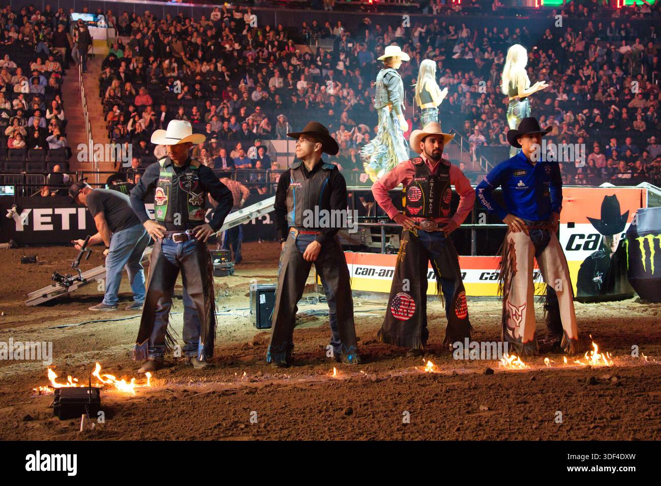 Four rodeo cowboys stand in a dirt arena with flames at their feet ...