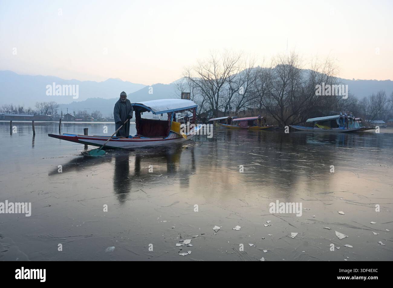 SRINAGAR, INDIA - JANUARY 9: A boatman rows his boat as he breaks ice ...