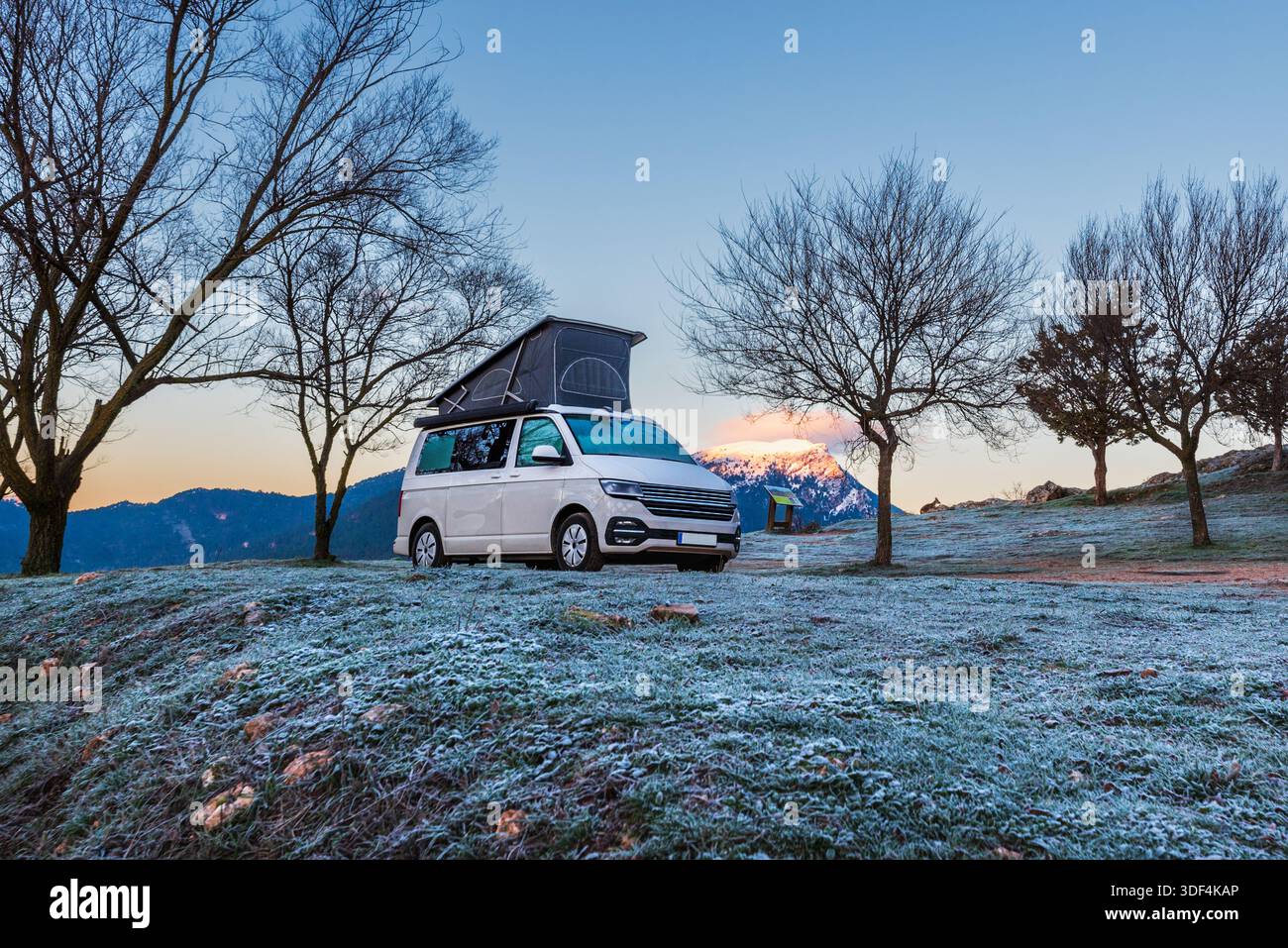 Camper van parked in nature on a winter morning with frozen ground and ...