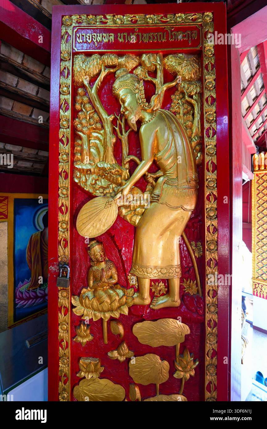 Traditional Lanna-style golden wood carving on a red temple door of the ...