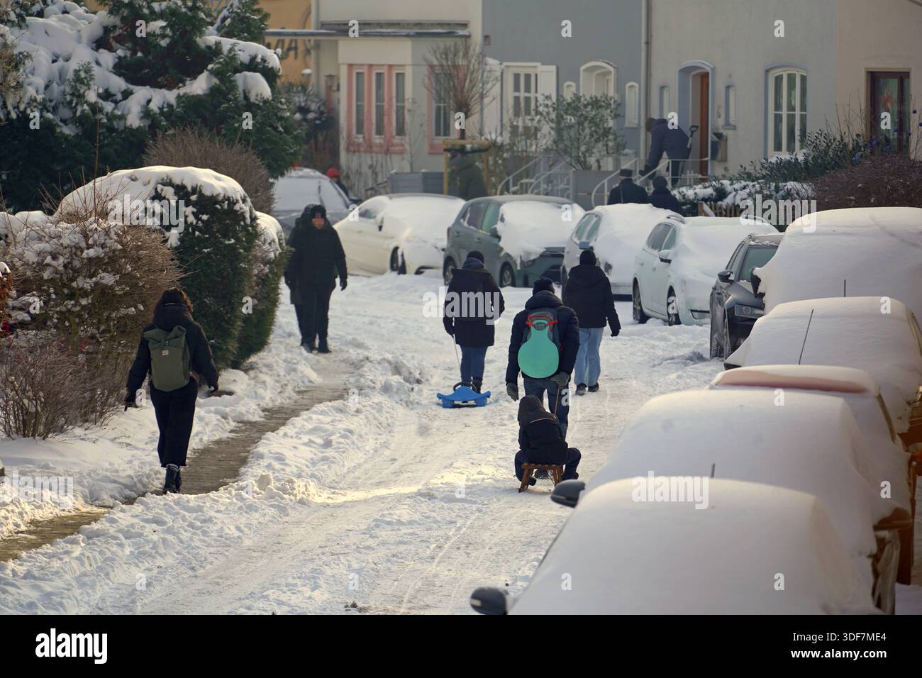 Junge Leute mit Schlitten und Spaziergänger auf einer zugeschneiten ...
