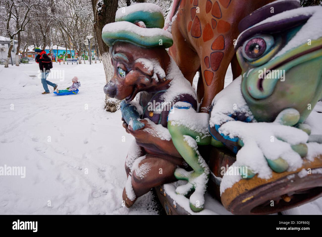A man pulls a child in a sled during a snowfall in a park, in Bucharest ...