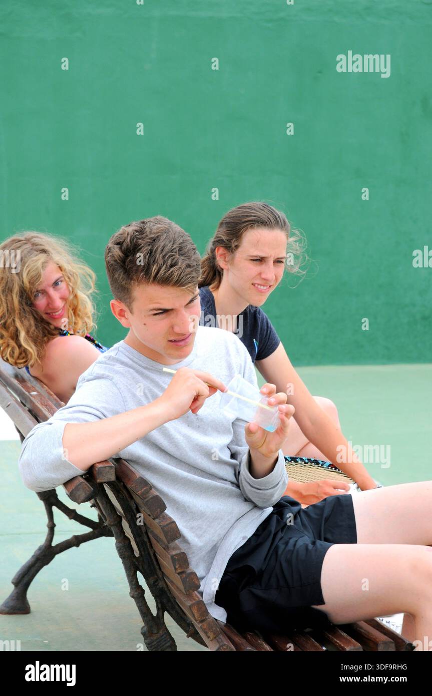 Three young people sitting on outdoor benches at a sports facility ...