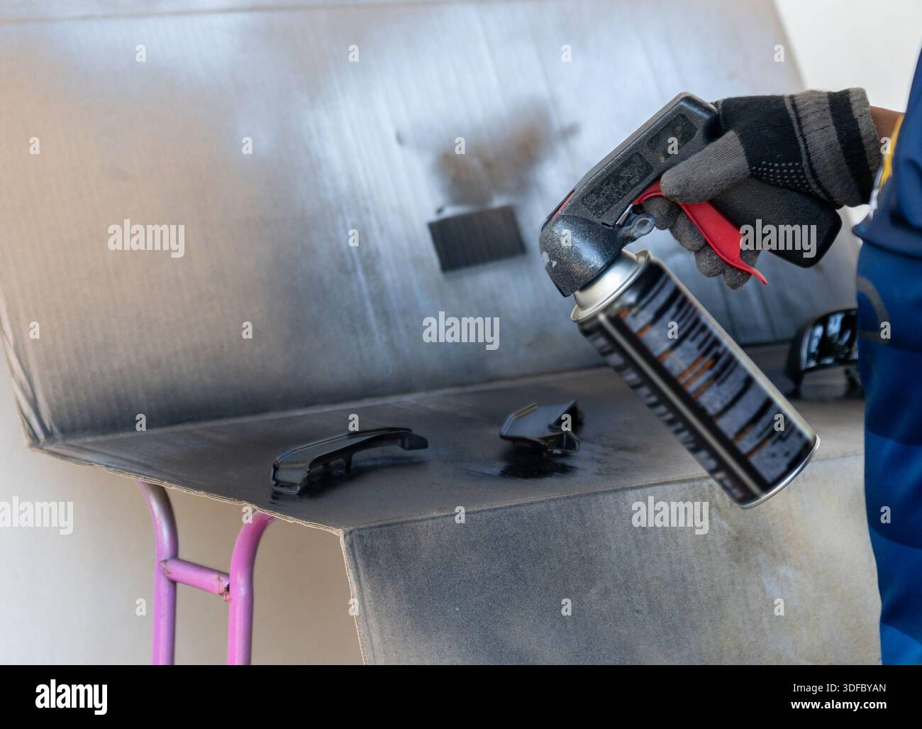 A person wearing protective gloves uses a black aerosol spray paint can ...