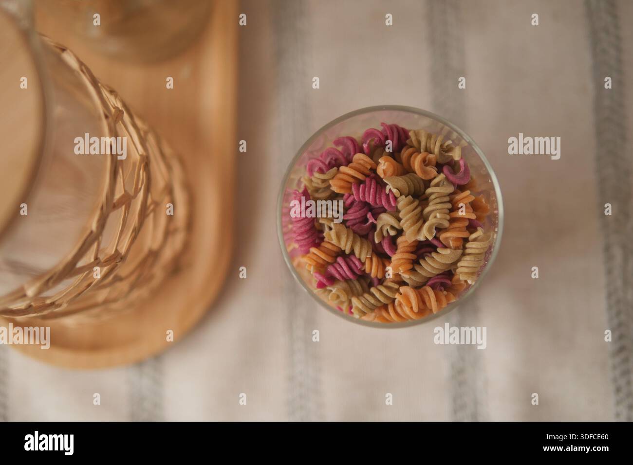 Colored pasta in a glass bowl on a table with wooden tray Stock Photo ...