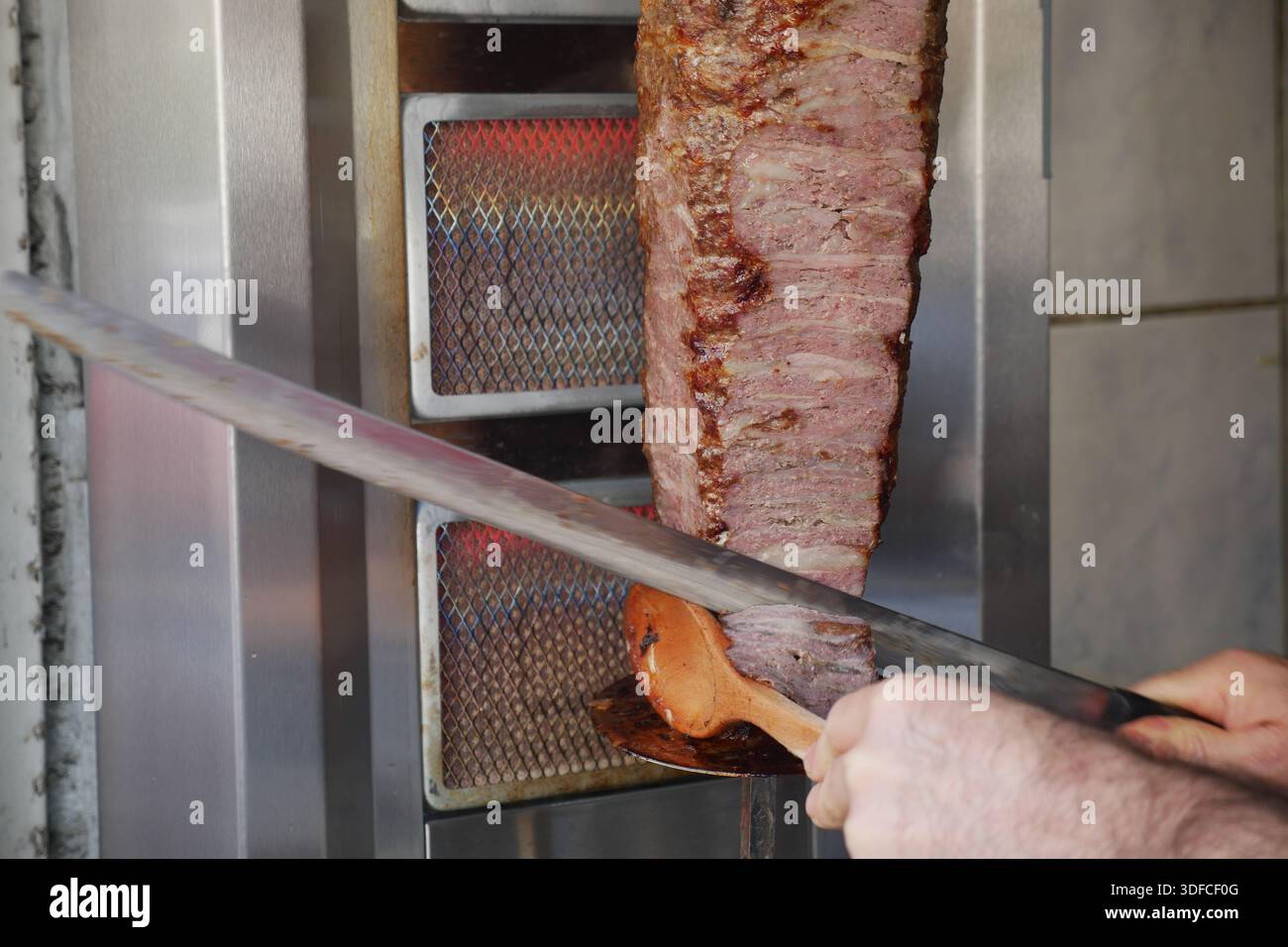 Chef slices meat from vertical grill in street food stall Stock Photo ...