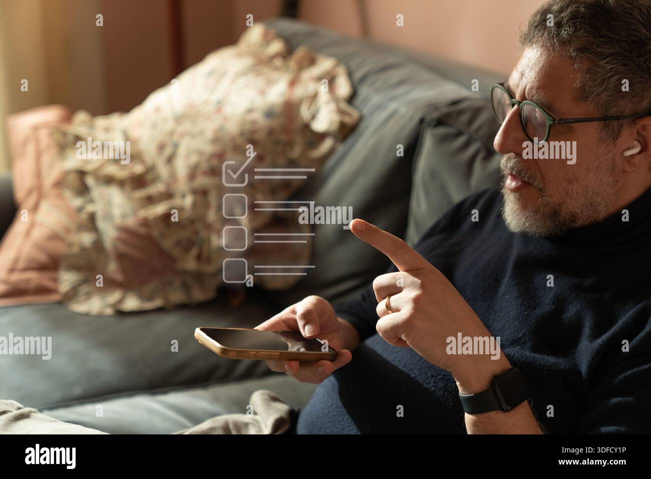 Middle aged man sitting on a sofa at home using a smartphone, making a ...