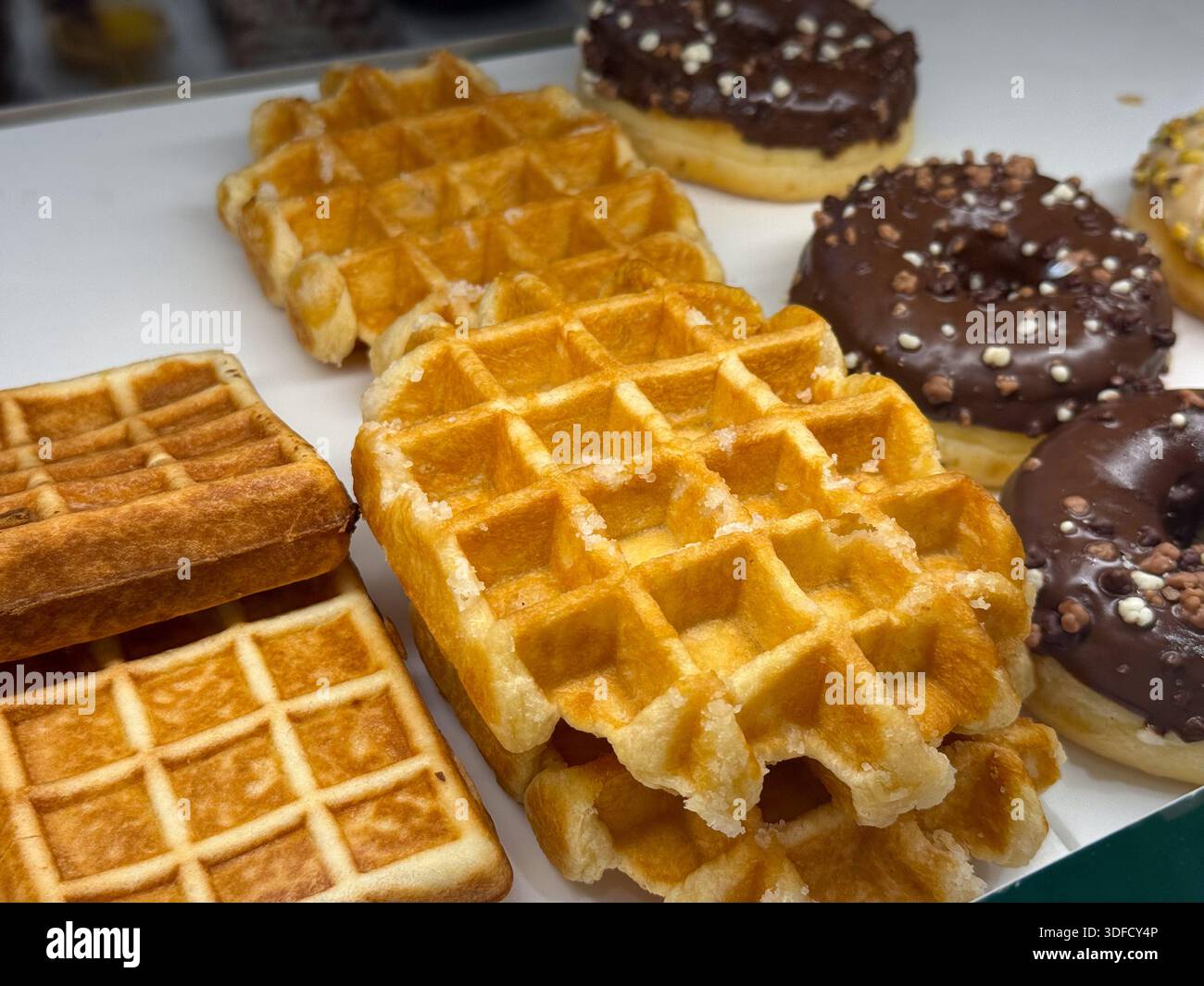 Belgian waffles and chocolate glazed donuts in bakery display. Sweet ...