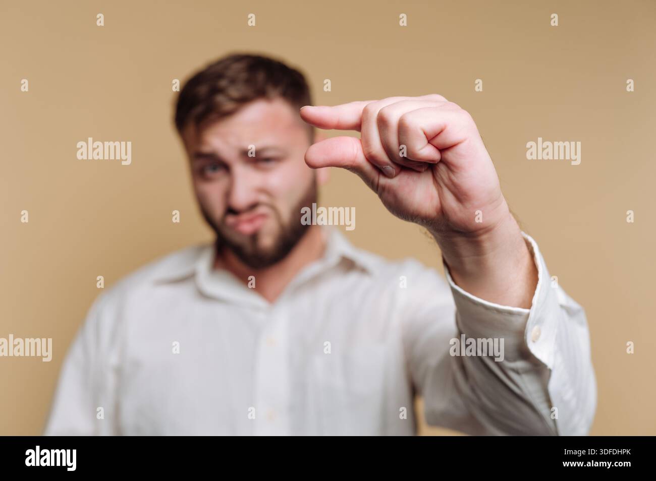 A man stands indoors, wearing a light shirt. He makes a hand gesture to ...